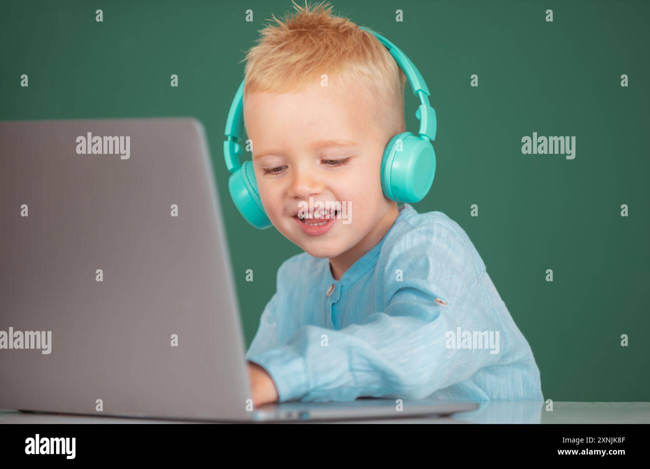 Clever school boy, cute pupil wears headphones writing on laptop ...