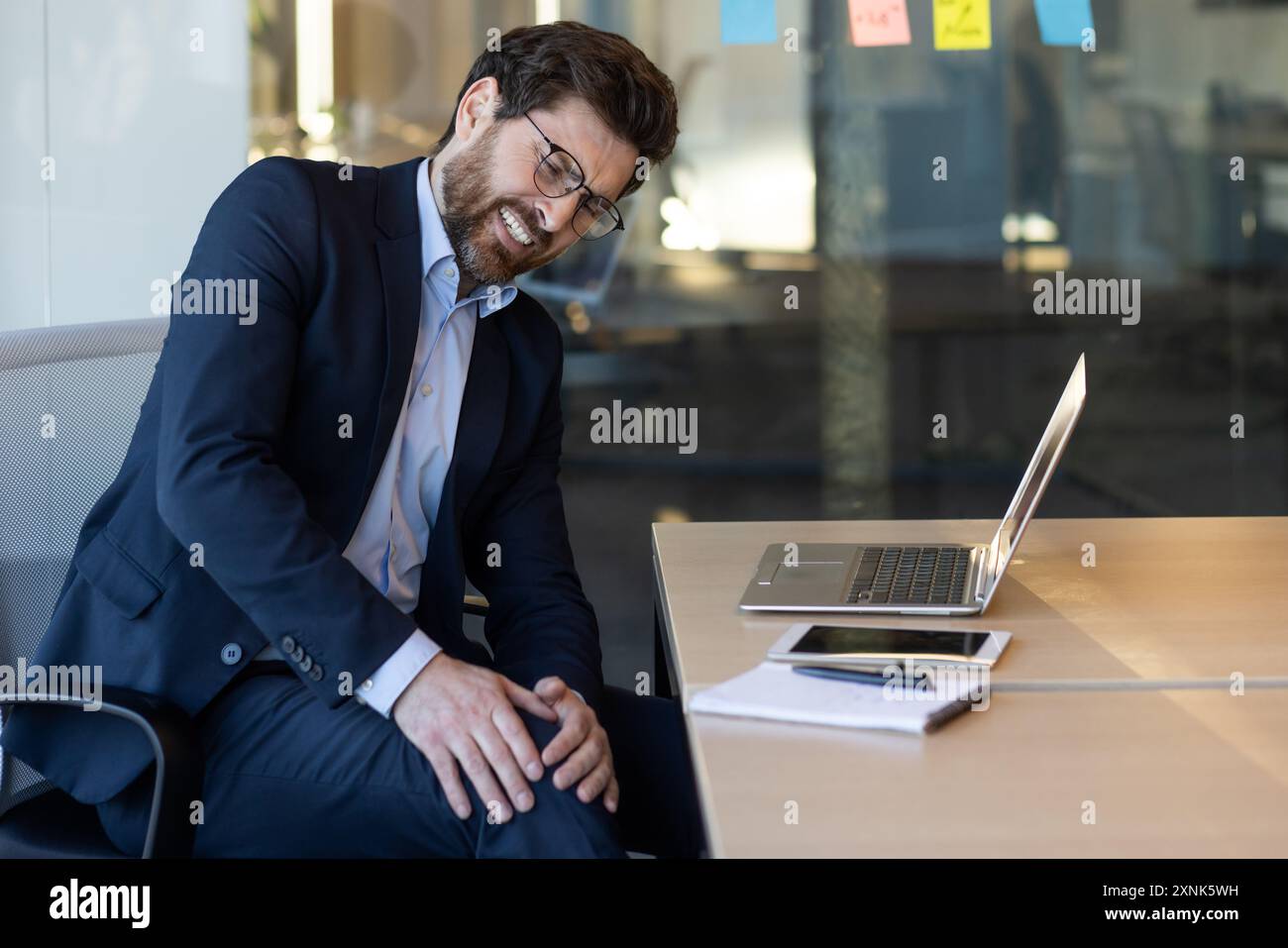 Businessman in formal attire experiencing leg pain while seated at desk ...