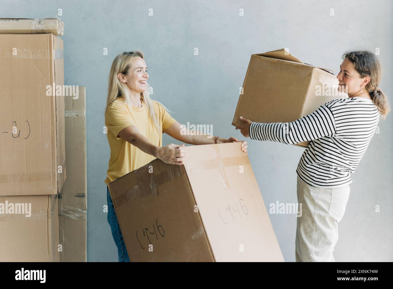 Happy women having fun loading boxes and stuff while moving to a new ...