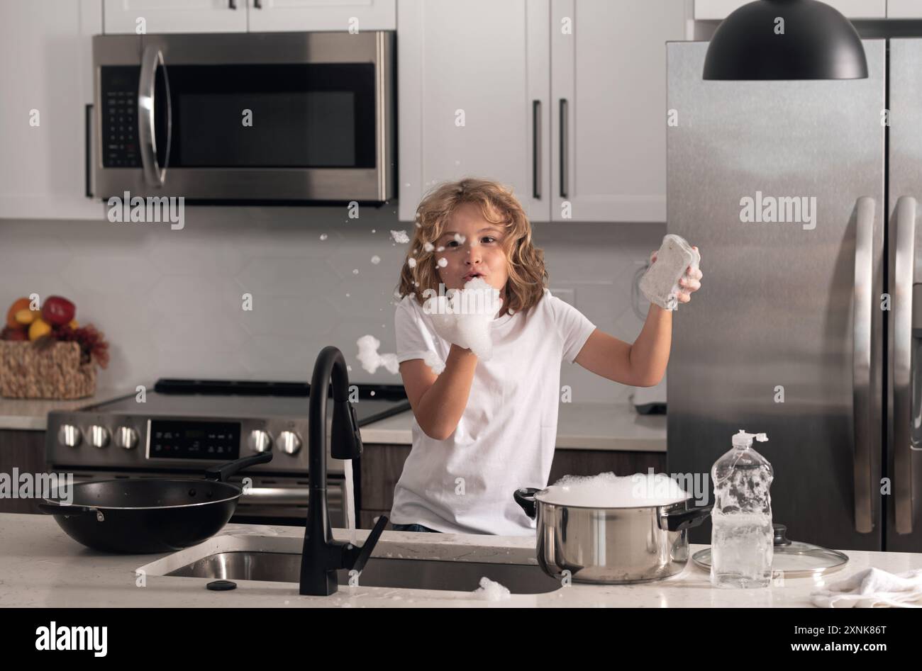 Child boy washing the dishes in the kitchen sink. Dishwashing liquid ...