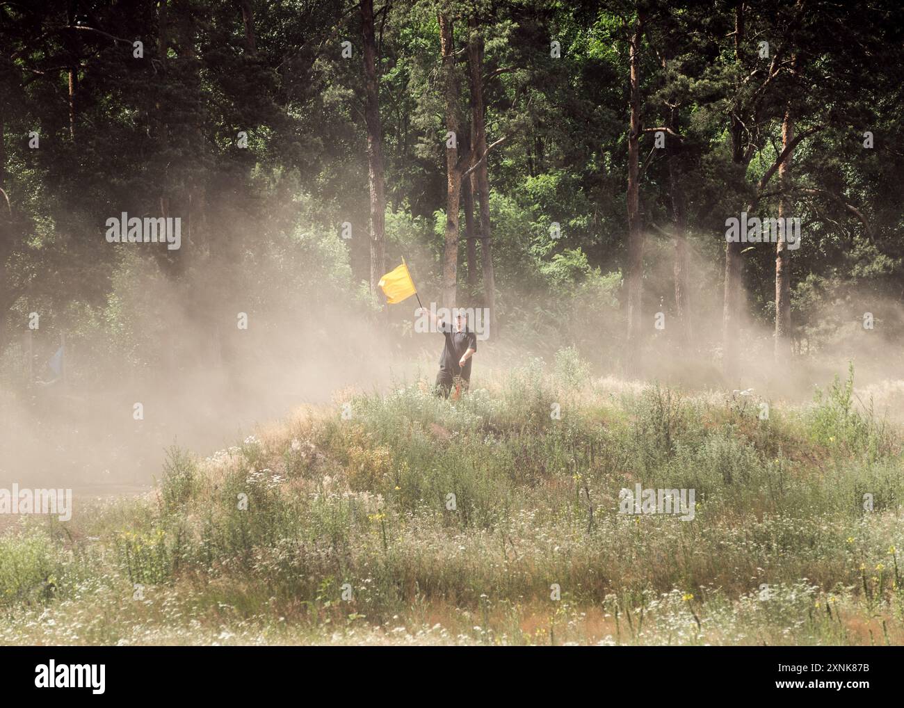 Man waving yellow flag in a forest clearing amidst dust, indicating ...