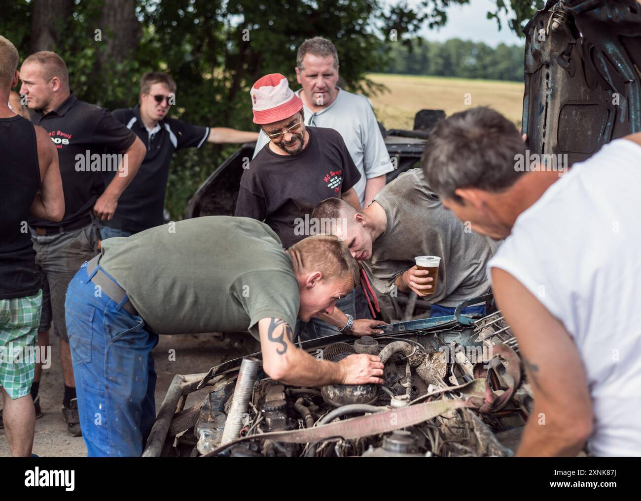 Group of men working collaboratively on a car engine at a demolition ...