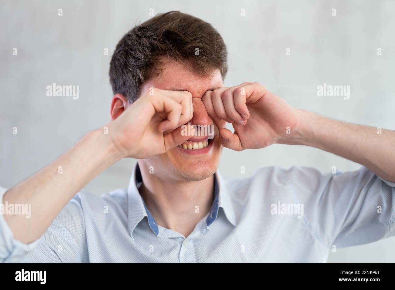 Man scretching itchy eyes on gray background Stock Photo - Alamy