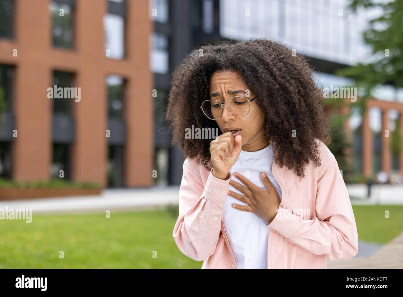 Woman with glasses and curly hair outdoors coughing and touching her ...