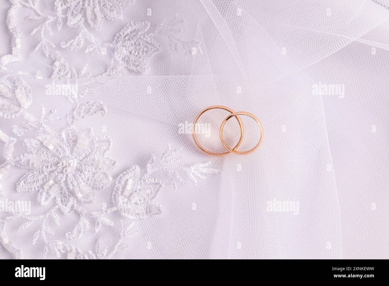 Two gold wedding rings are lying on a white embroidered veil. white ...