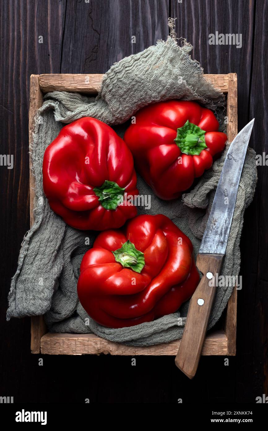 Fresh red sweet bell peppers in wooden box with knife on rustic table ...