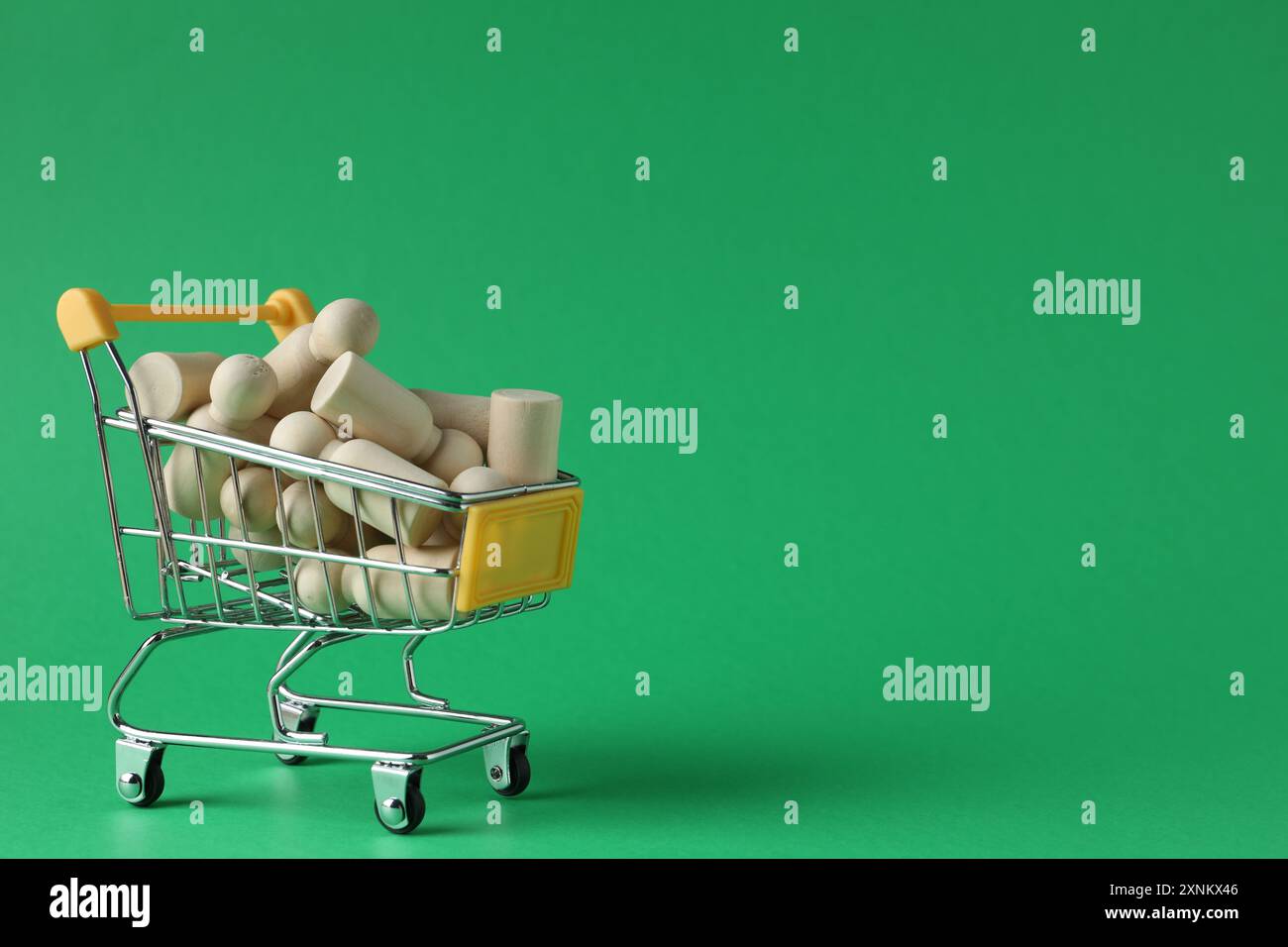 Wooden human figures in small shopping cart on green background, space ...