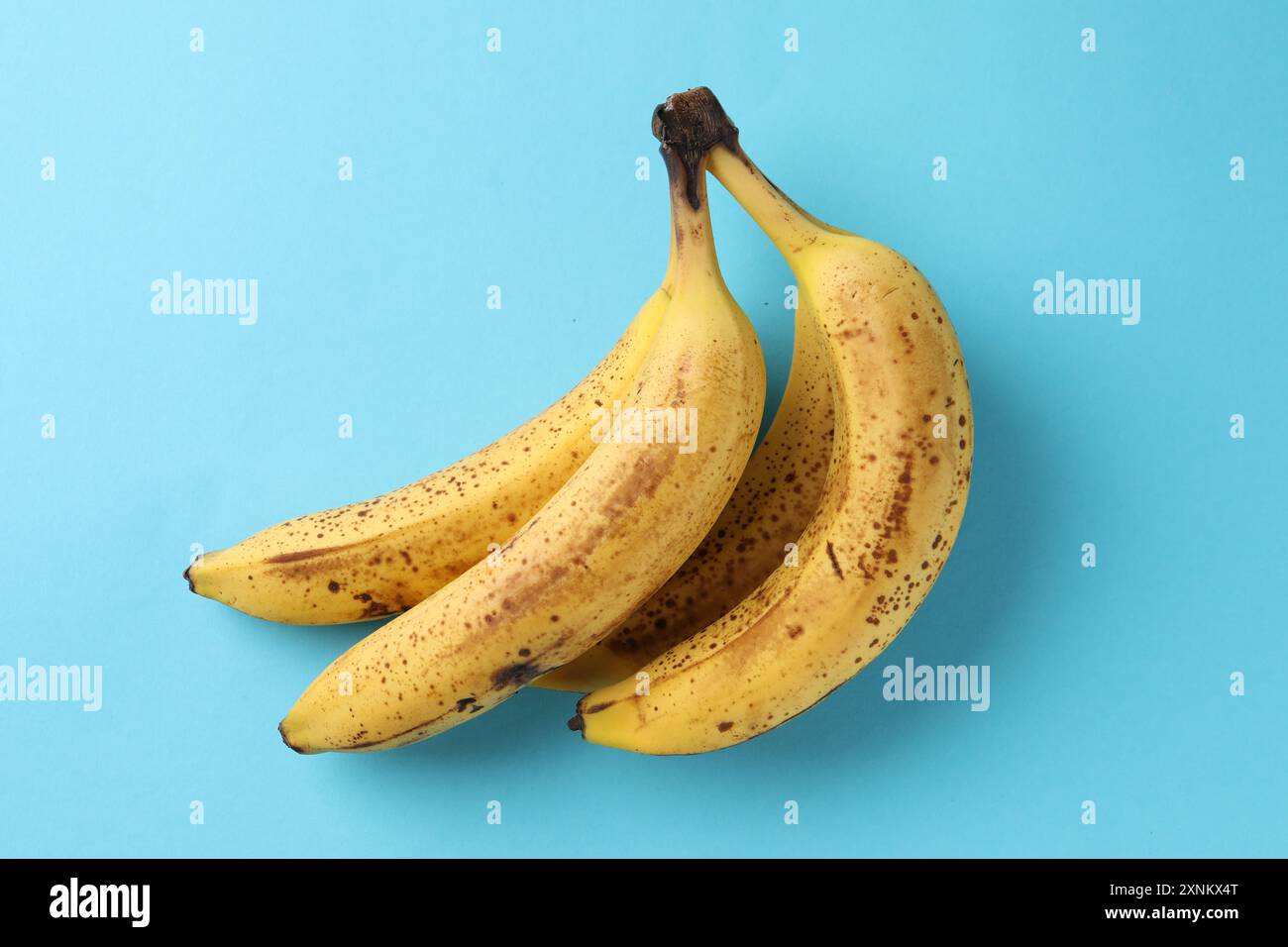 Bunch of ripe bananas with dark spots on light blue background, top ...