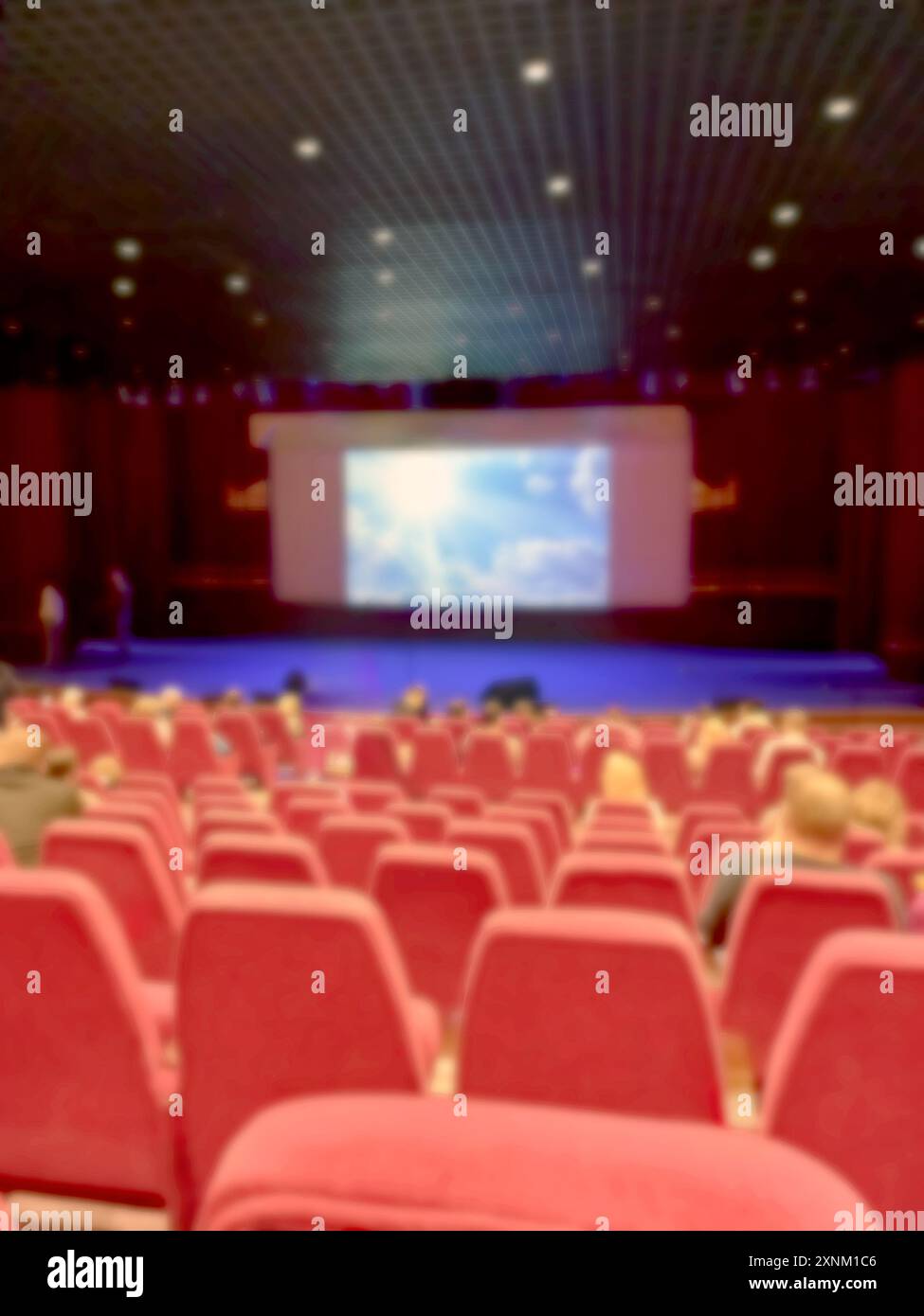 Auditorium with red seats and screen at beginning of show. Blurred for ...