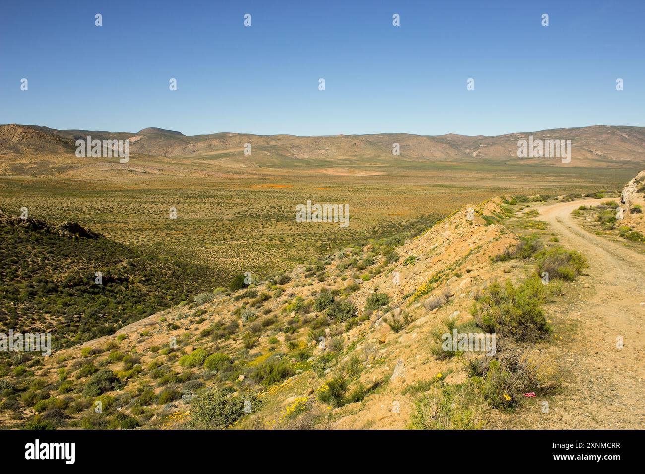 A small dirt road, going over a mountain pass in the arid scrublands of ...