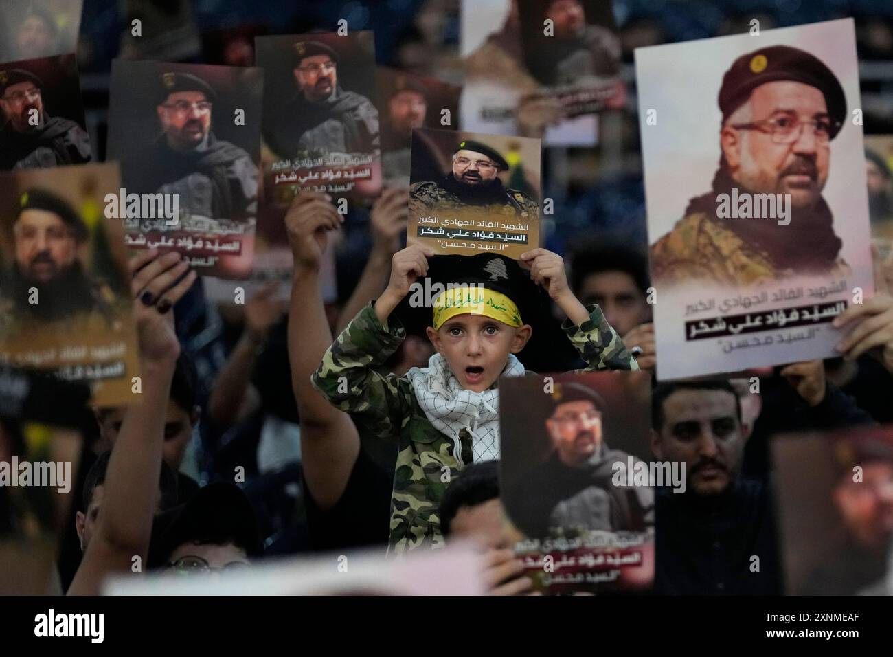 A boy holds up a portrait of Hezbollah commander Fouad Shukur, who was ...
