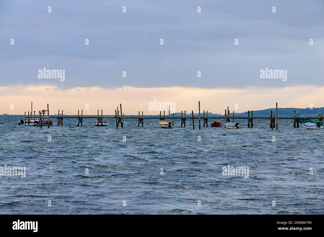 Boats gently sway in the water alongside an old wooden dock, with a ...