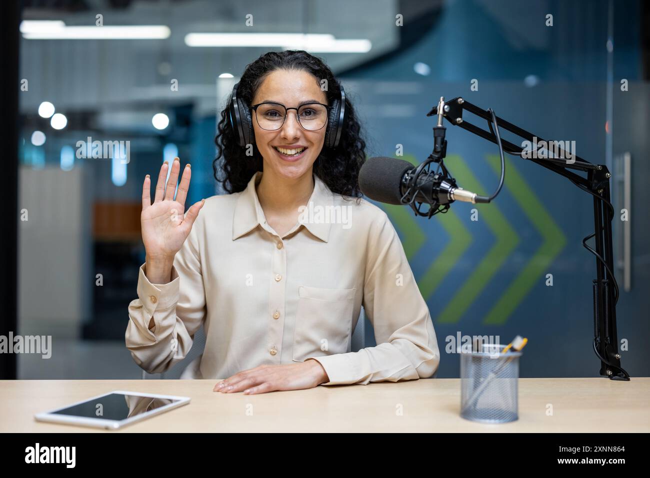 Smiling podcast host with headphones waving to camera in professional ...