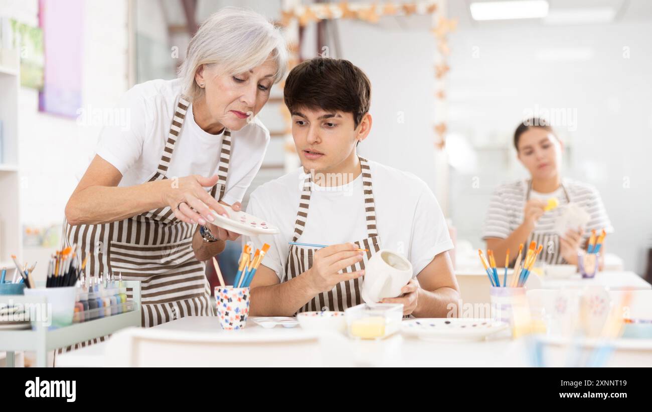 Experienced female ceramicist teaching enthusiastic guy to paint ...