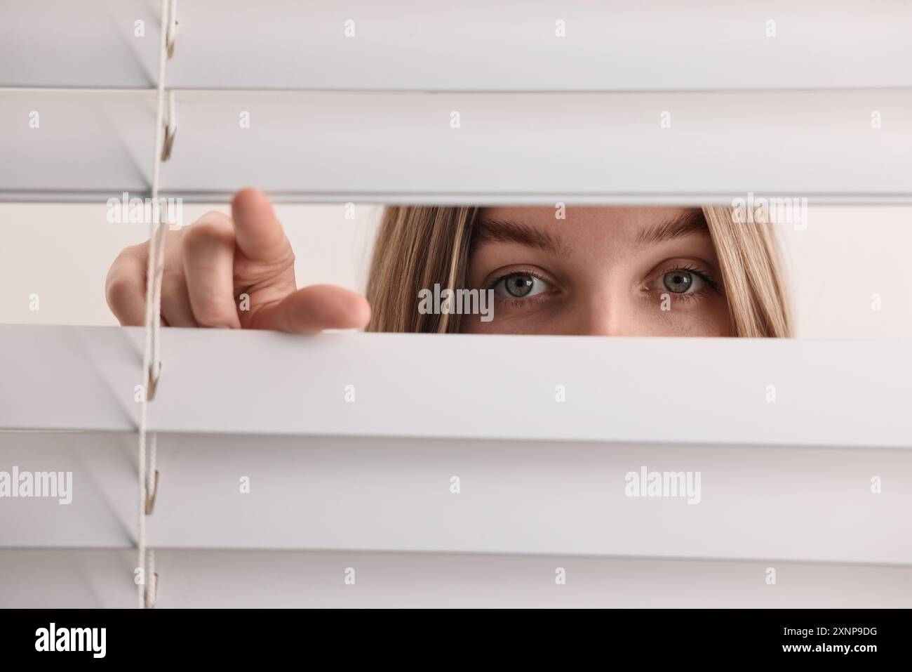 Young woman looking through window blinds on white background Stock ...