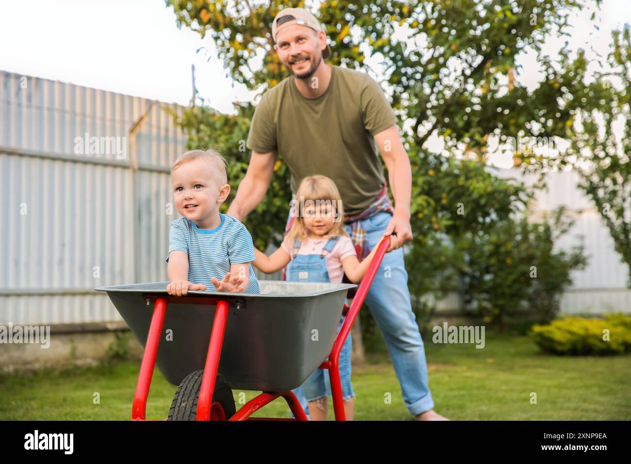Father pushing wheelbarrow with his kids outdoors, space for text Stock ...