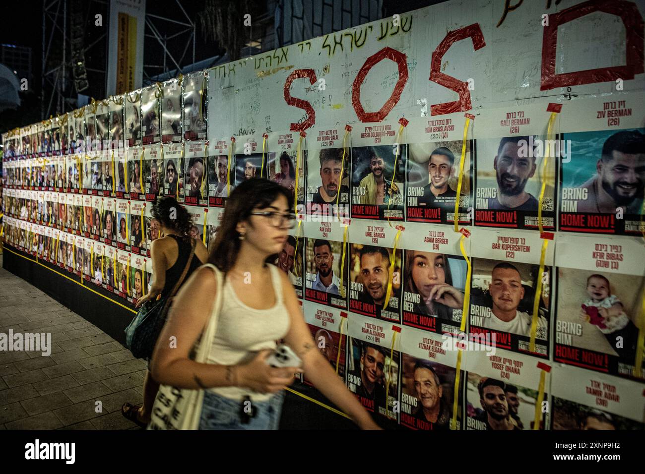 An Israeli woman walks past a billboard covered with images of hostages ...