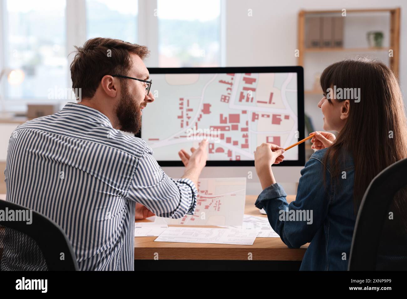 Cartographers working with cadastral maps at table in office, back view ...