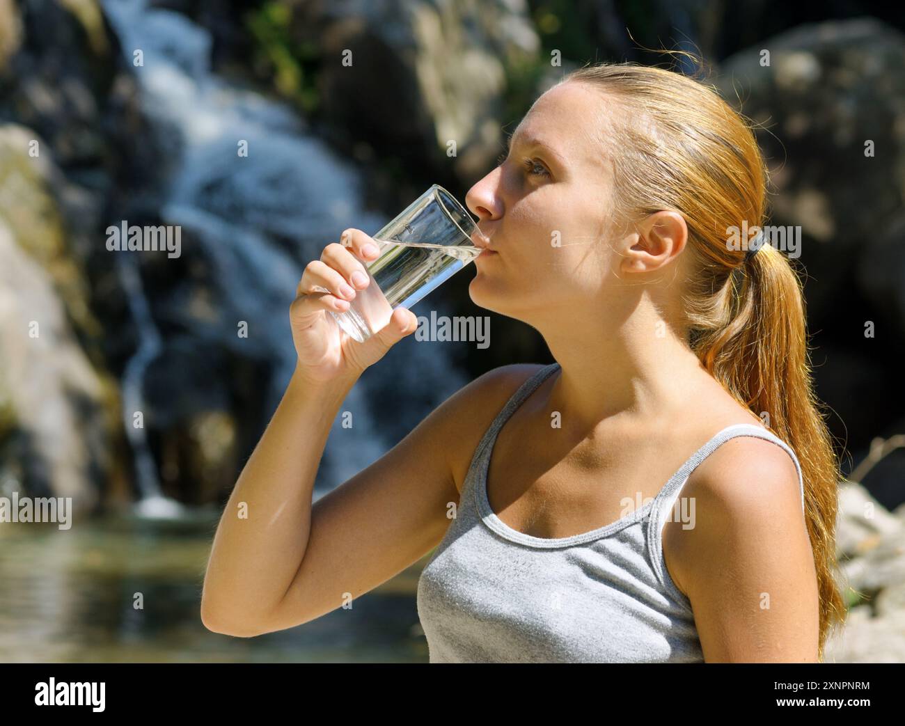 Young woman drinks water by waterfall Stock Photo - Alamy