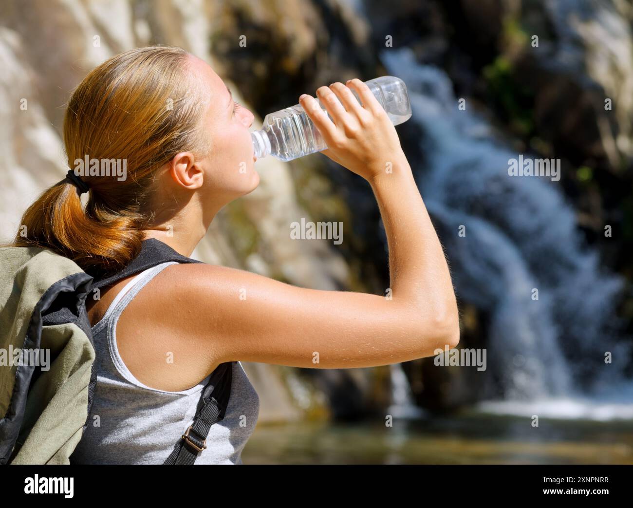 Young woman drinks water by waterfall Stock Photo - Alamy