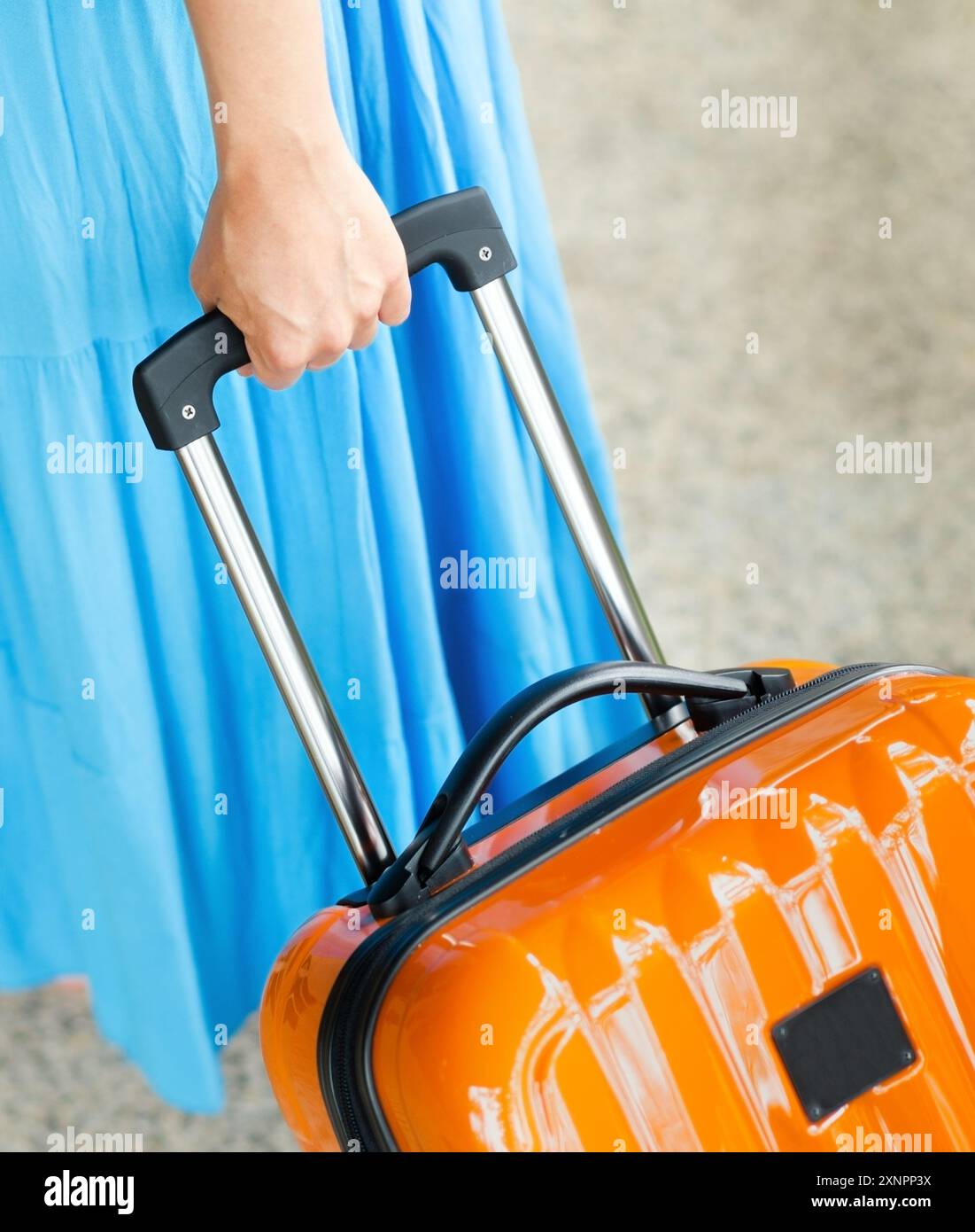 Woman in blue dress holds orange suitcase in hand Stock Photo - Alamy