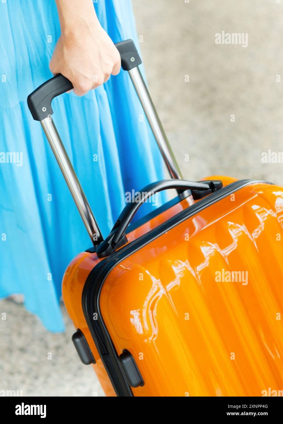 Woman in blue dress holds orange suitcase in hand Stock Photo - Alamy