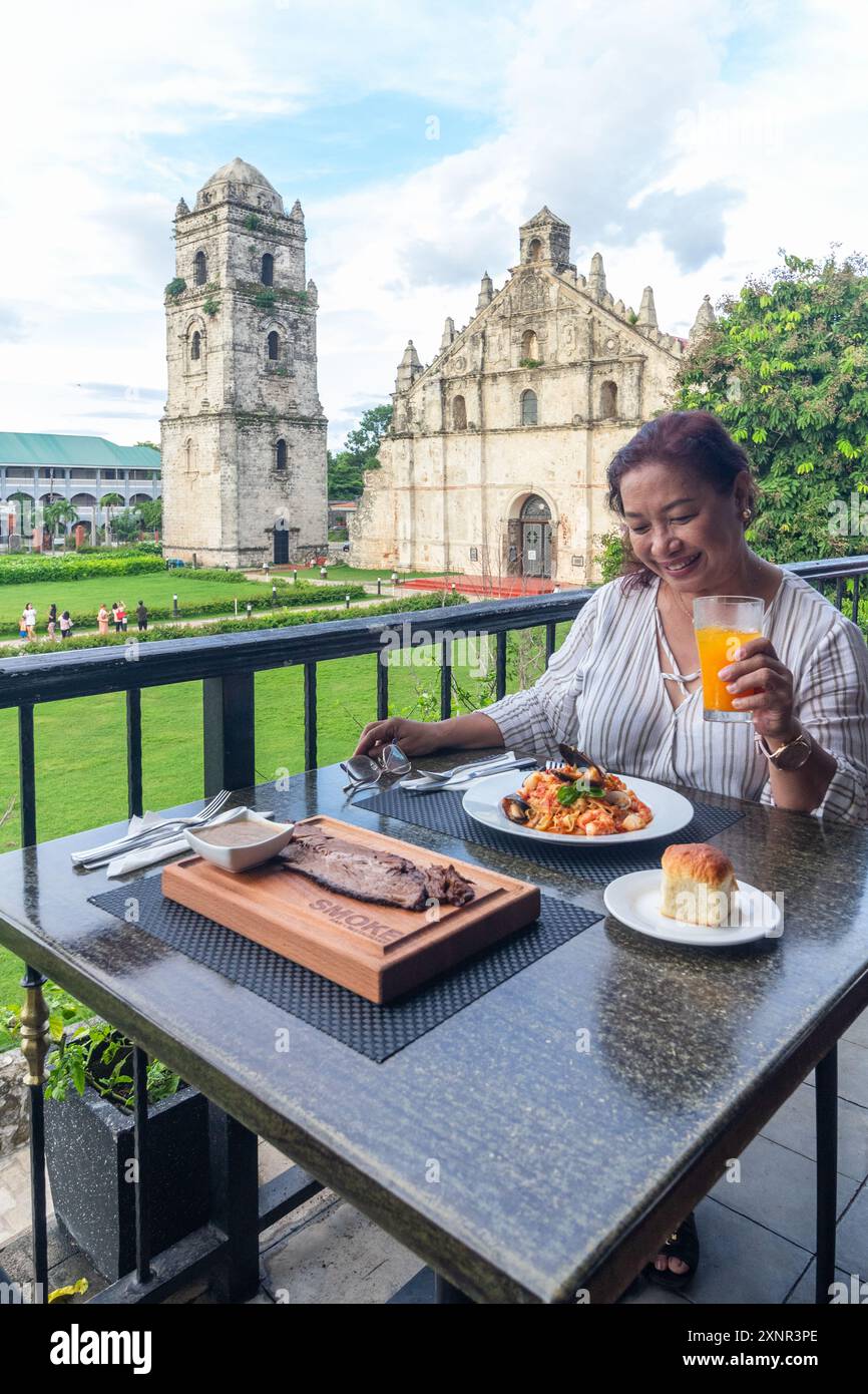 Woman eating at the veranda of a restaurant overlooking Paoay Church, a ...