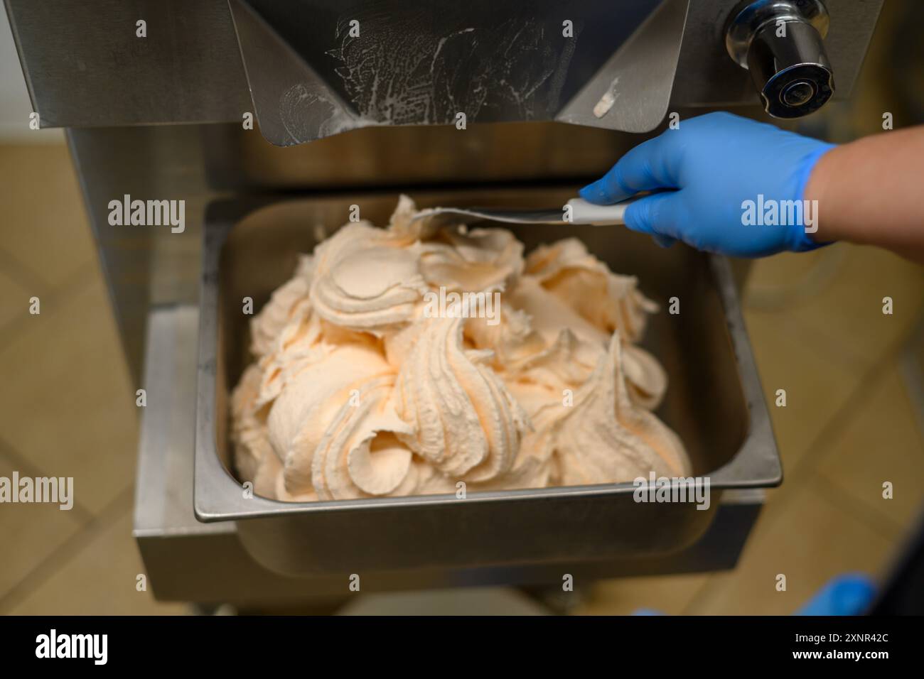 A close-up of a person using a spatula to scoop creamy gelato from a ...