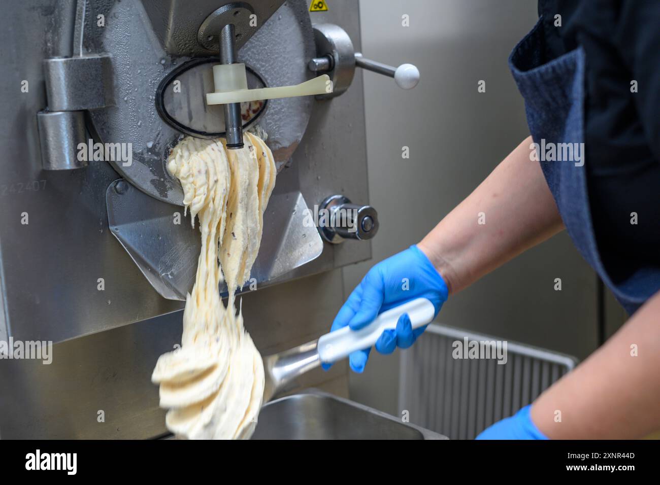 A person in blue gloves operates an ice cream machine, with creamy ice ...