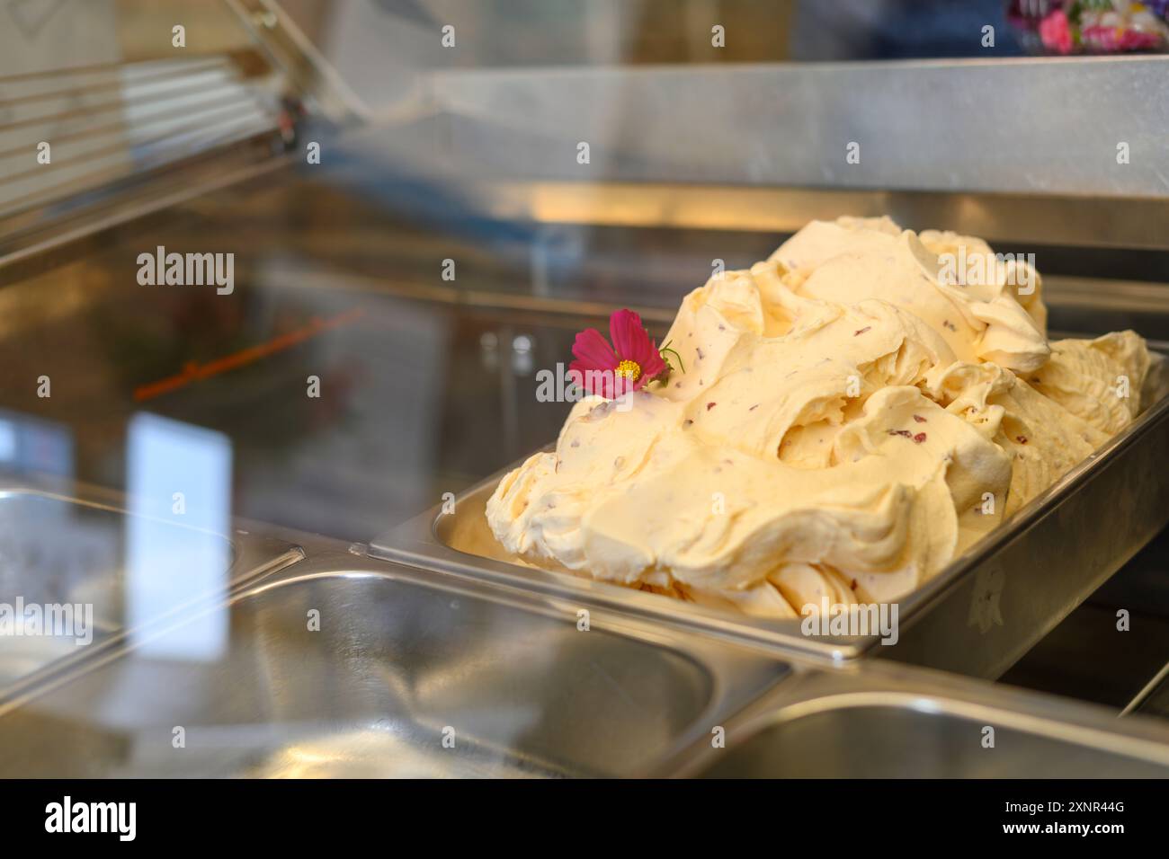 A close-up view of creamy gelato in a metal container, topped with a ...