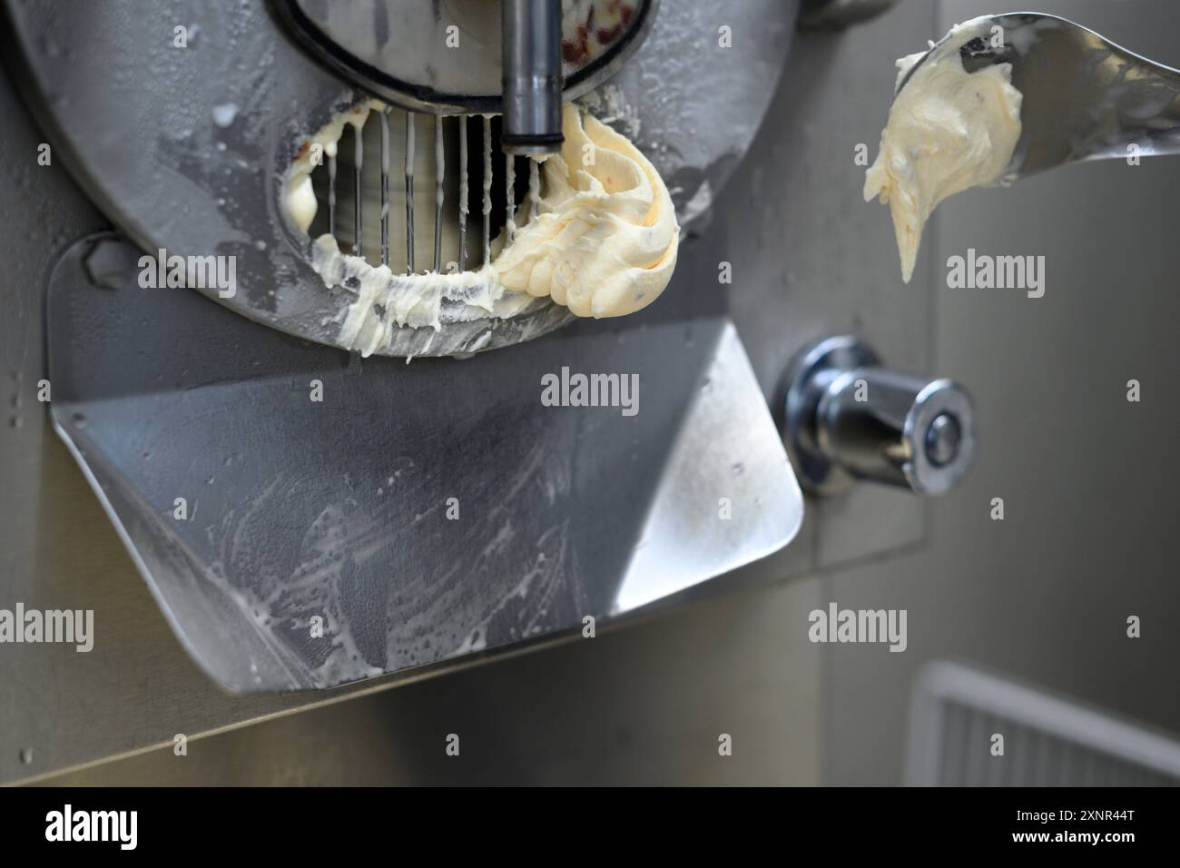A close-up of an ice cream machine dispensing creamy vanilla ice cream ...