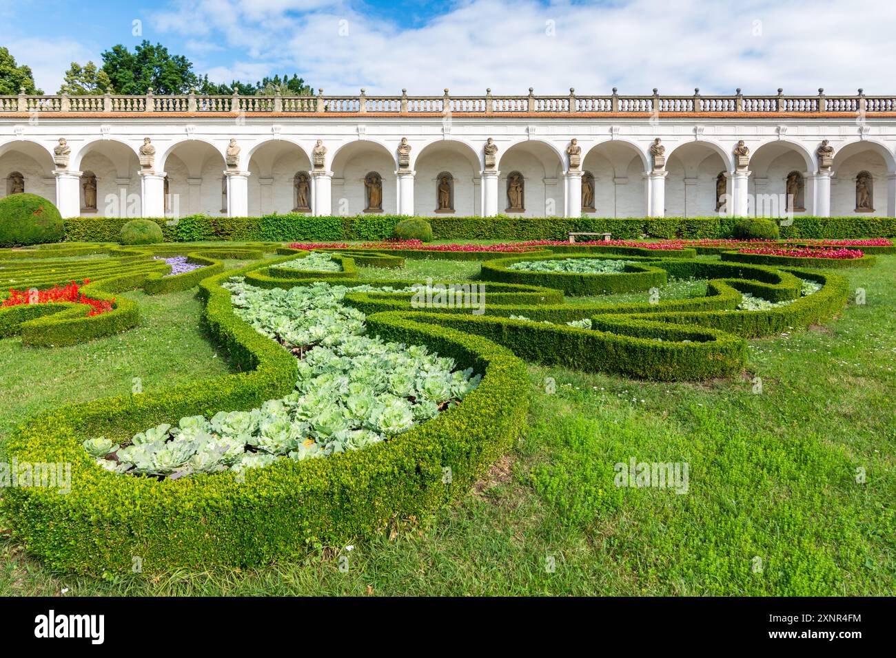 White baroque colonnade with statues of ancient gods in a flower garden ...
