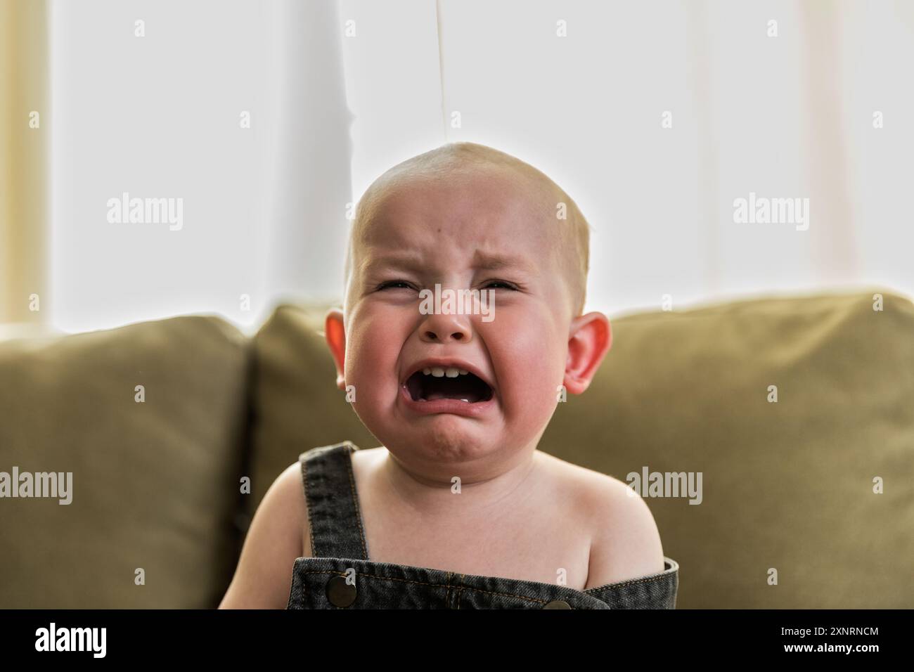 Little baby boy crying sitting on couch Stock Photo - Alamy