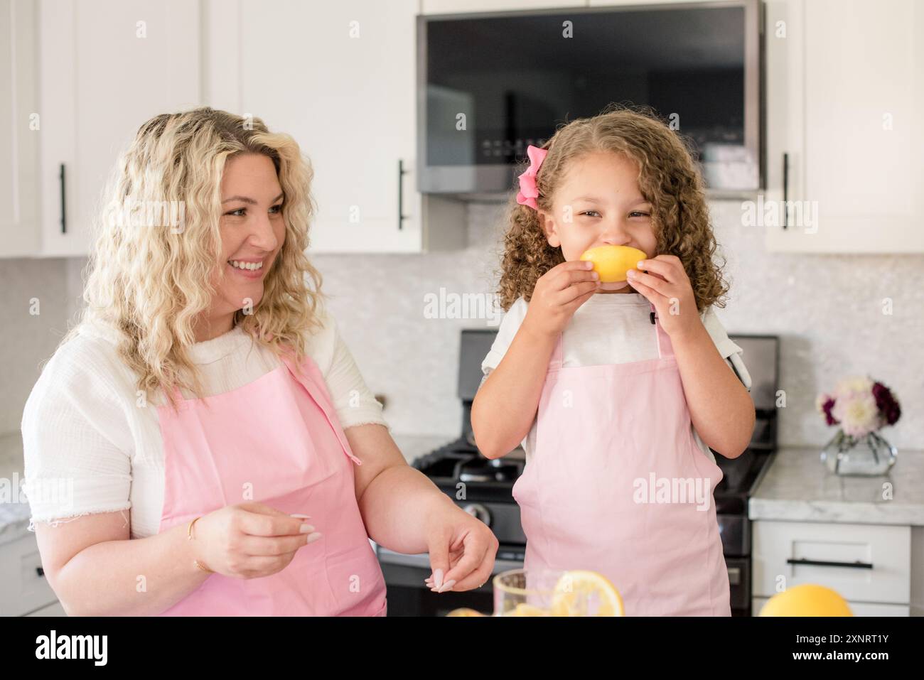 Little girl covering her mouth with lemon and mom watching Stock Photo ...