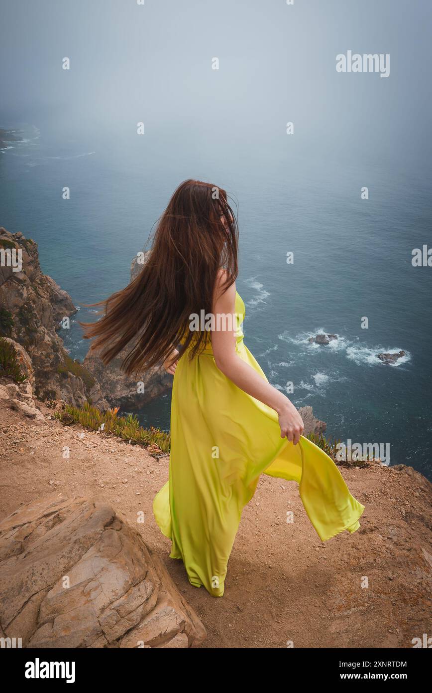 Woman in Yellow Dress on Misty Cliff Overlooking Atlantic Ocean at Cabo ...
