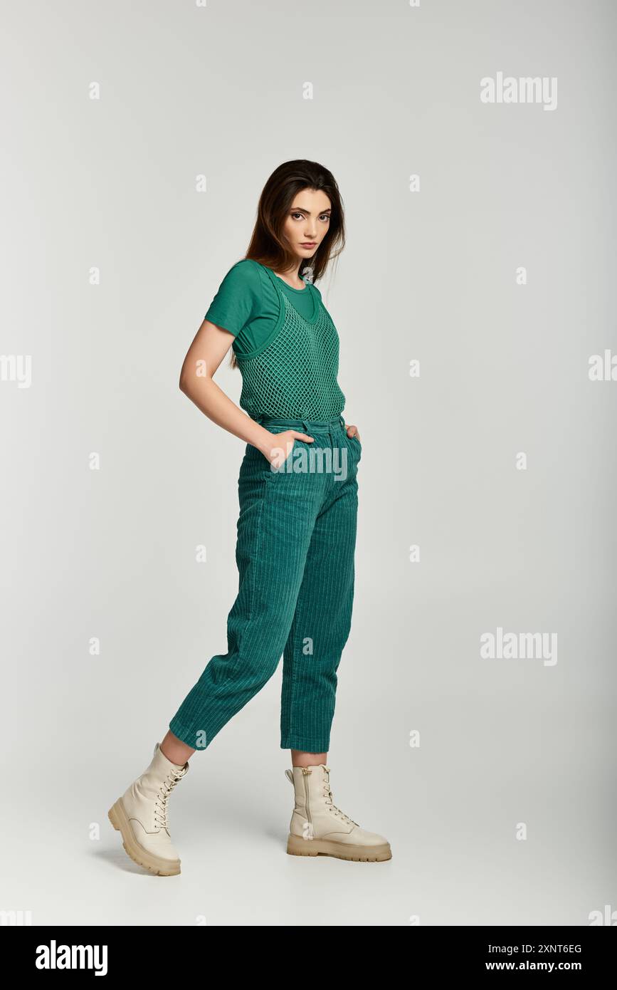 A young woman in a green outfit poses confidently against a white ...