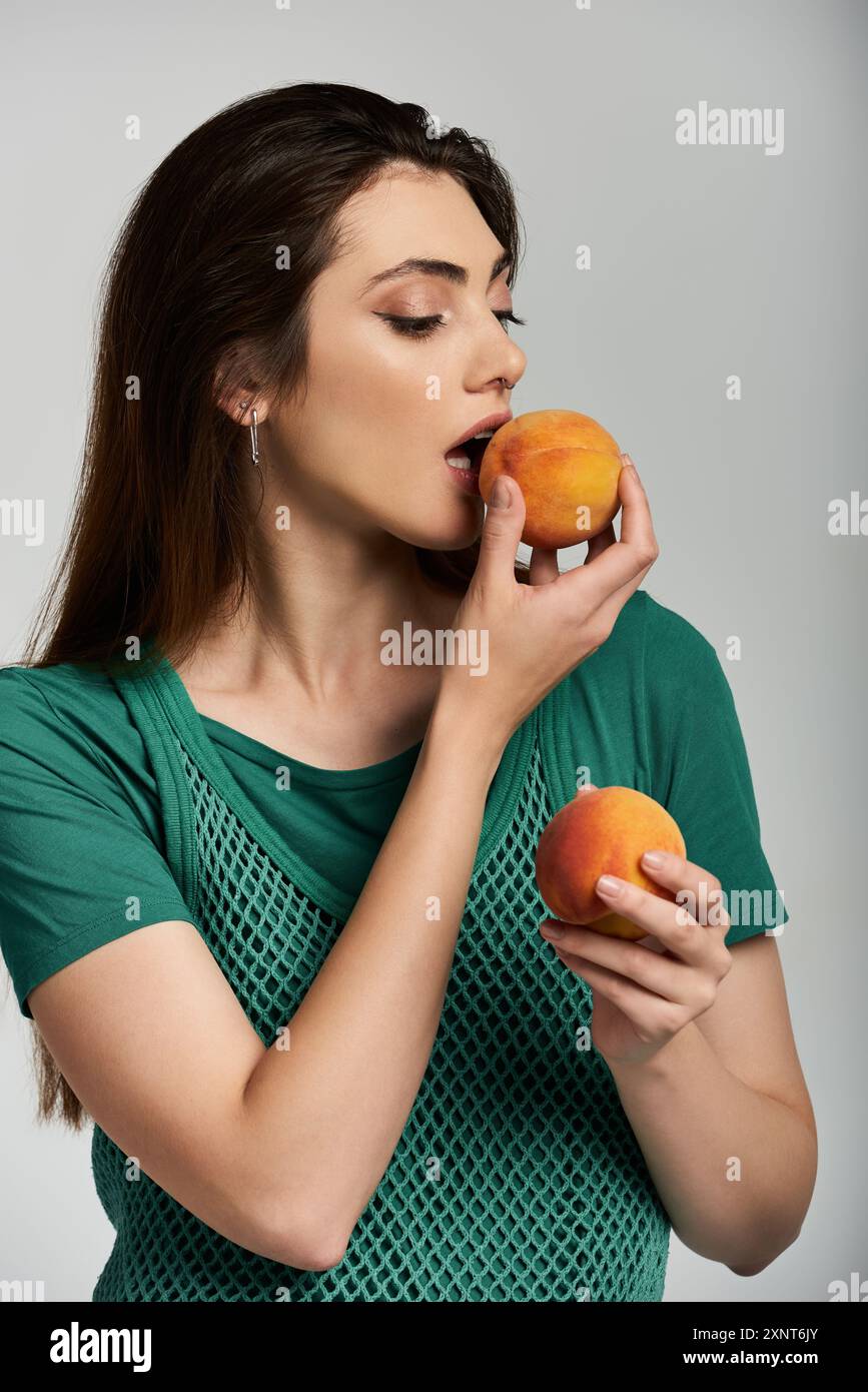 A young woman in a green mesh top takes a bite of a peach Stock Photo ...