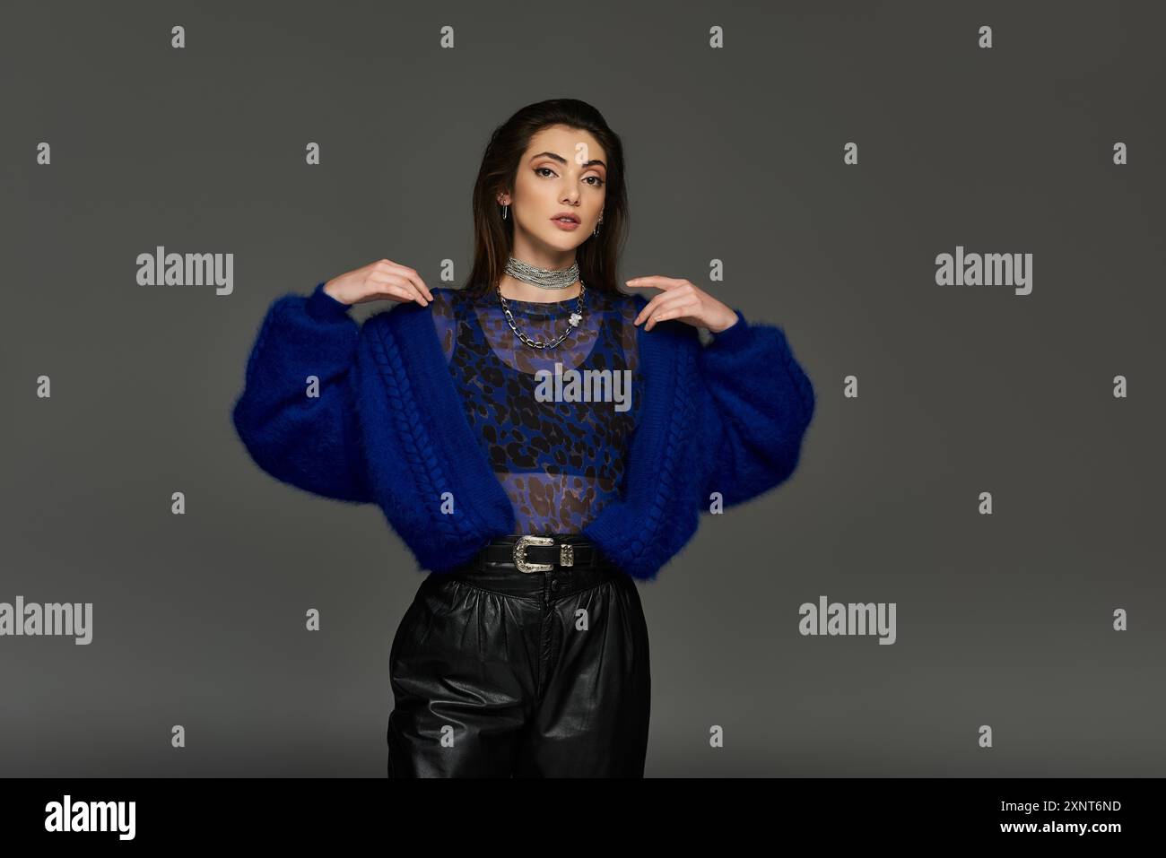 A young woman wearing a blue fuzzy cardigan poses against a gray ...