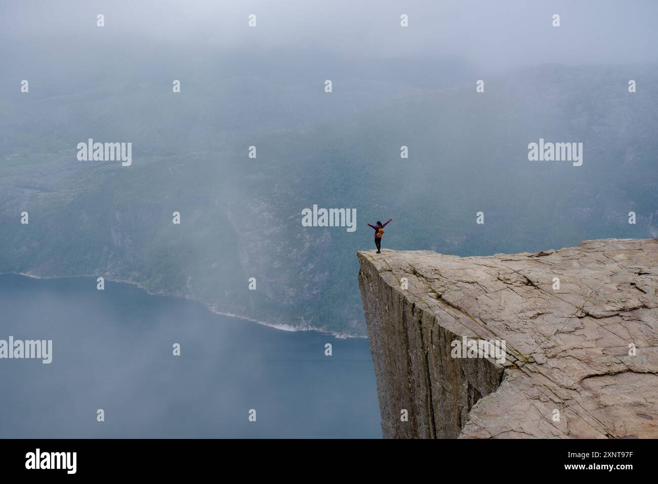 A solo hiker triumphantly poses at the precipice of Preikestolen ...