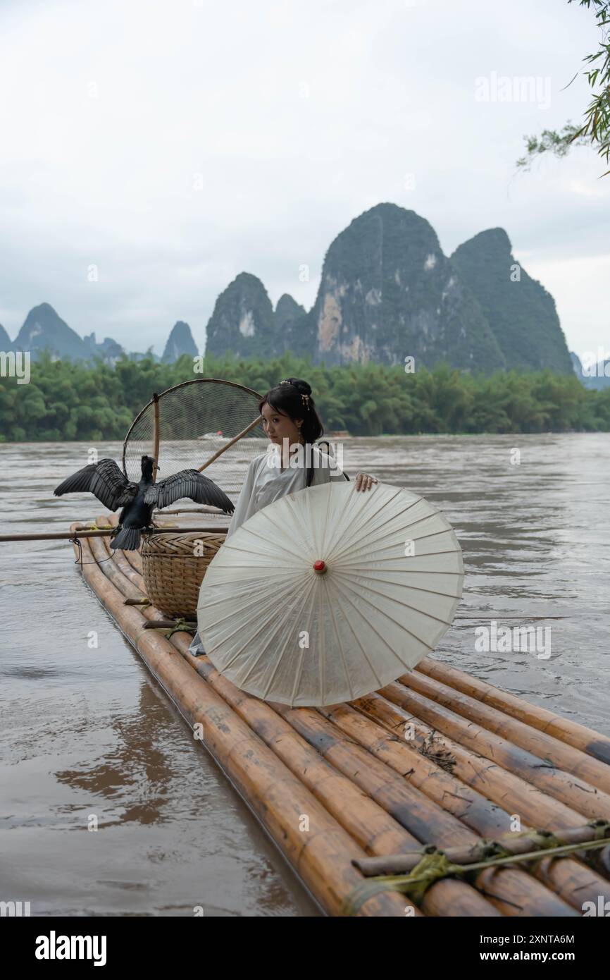 Hanfu girl with umbrella on bamboo raft in Xingping posing with ...