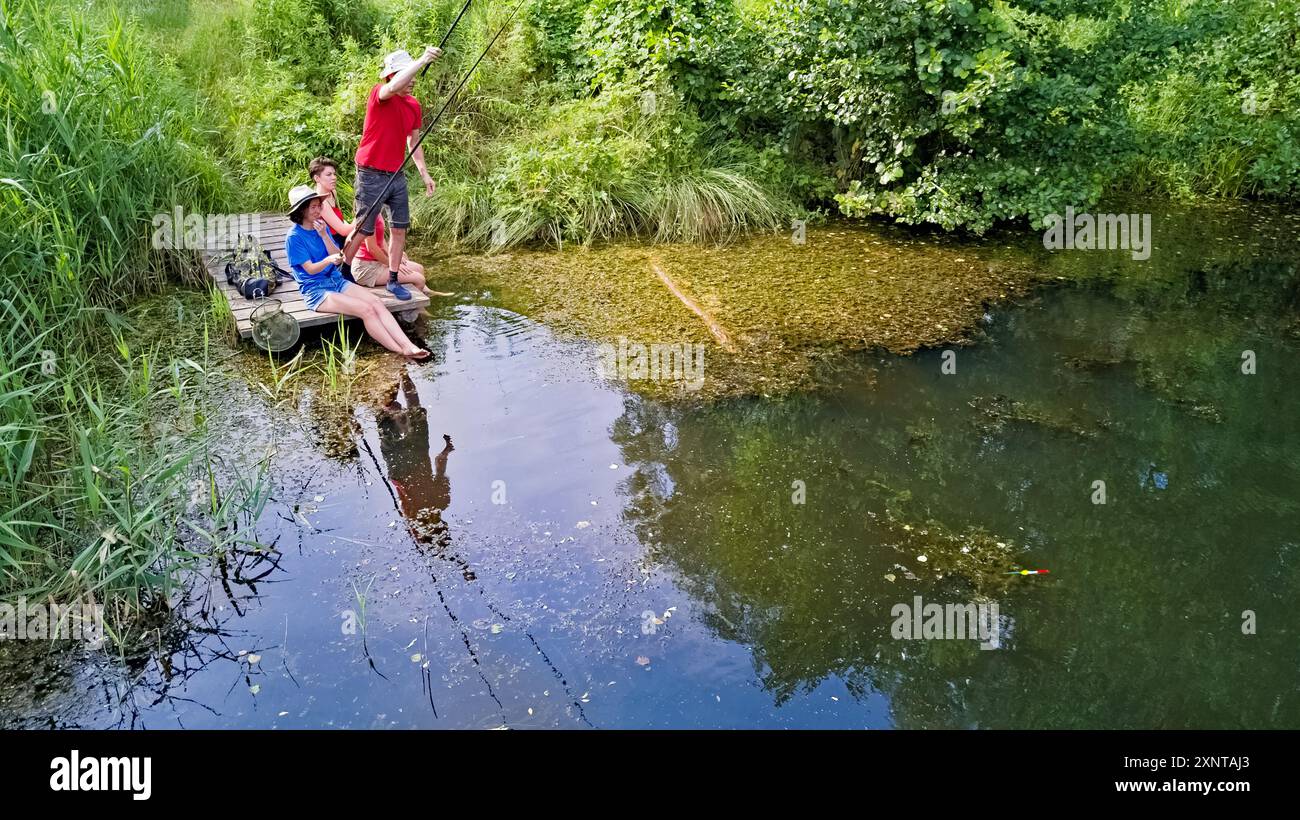 Happy family and friends fishing together outdoors near lake in summer ...