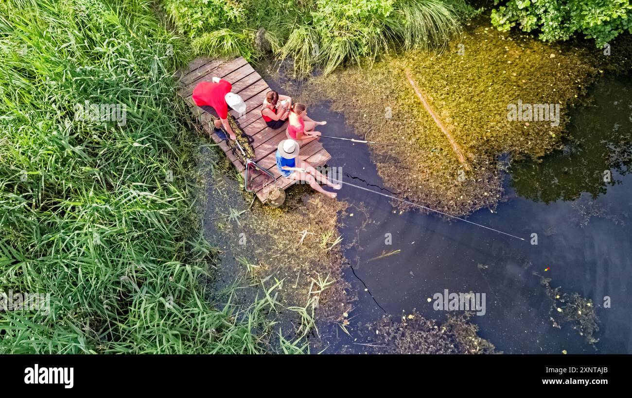 Happy family and friends fishing together outdoors near lake in summer ...