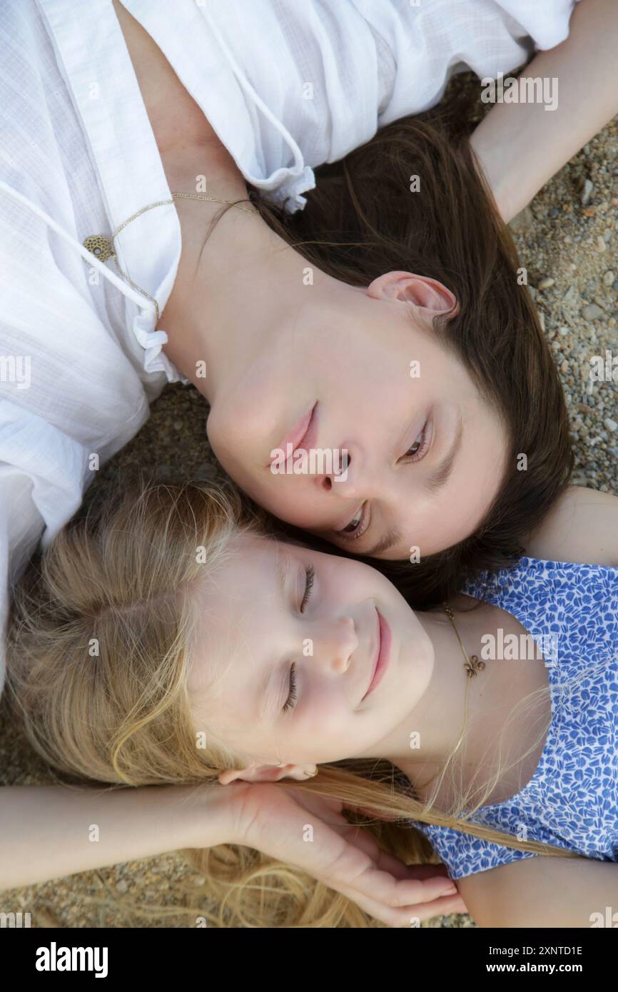 Happy little girl laying on the sand with her mother, top view. Happy ...
