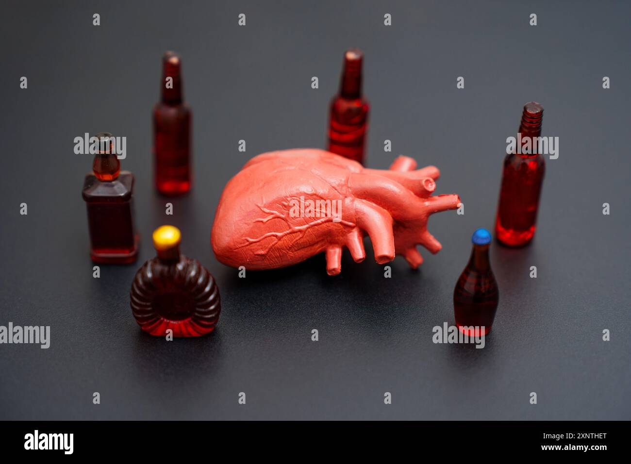 Red clay heart model positioned among various dark-colored alcohol ...