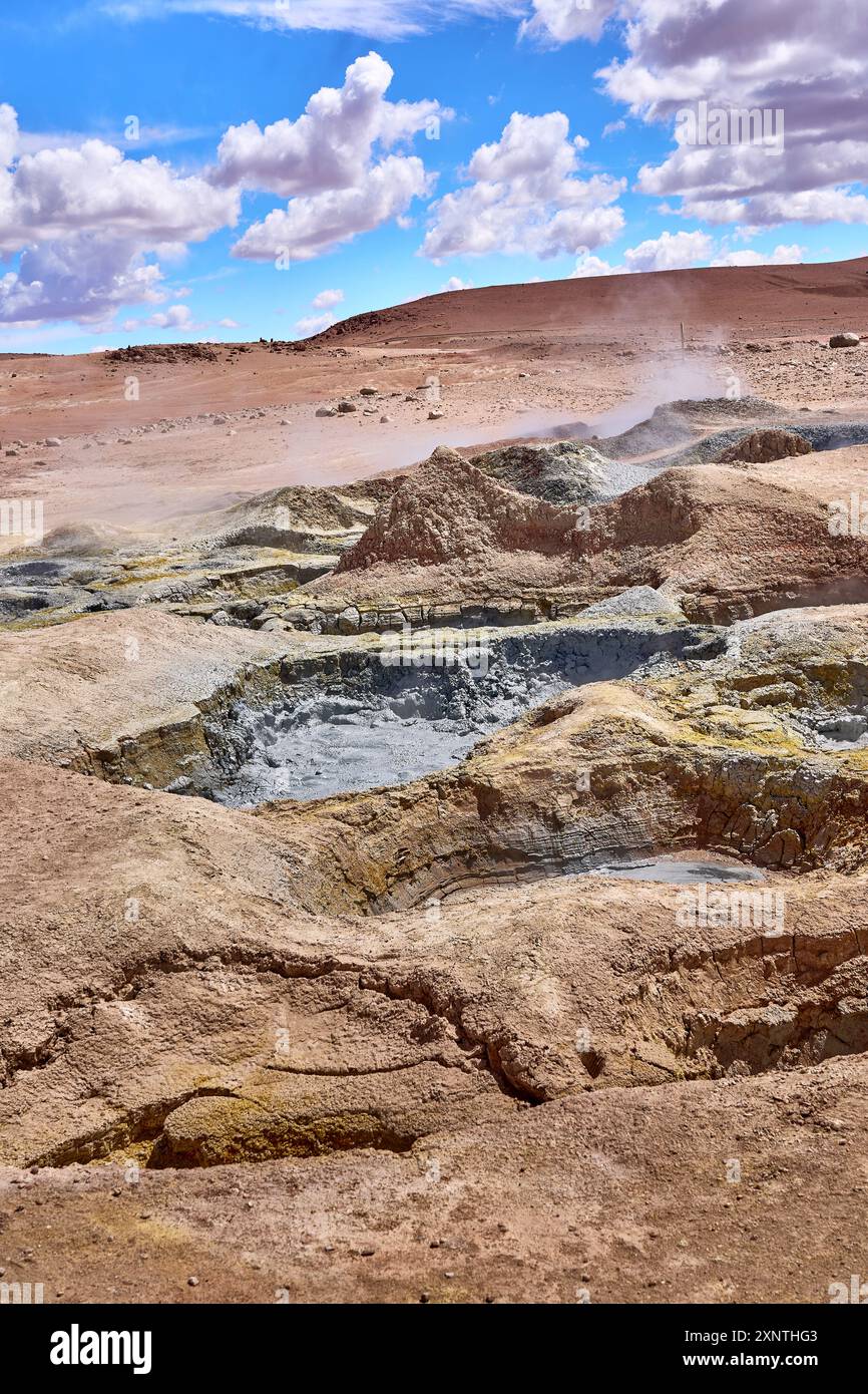 A steaming geothermal field in a desert landscape under a bright blue ...