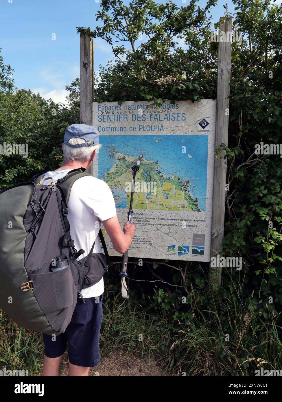 France, a hiker examining a map of the bay of Plouha, nestled in the ...