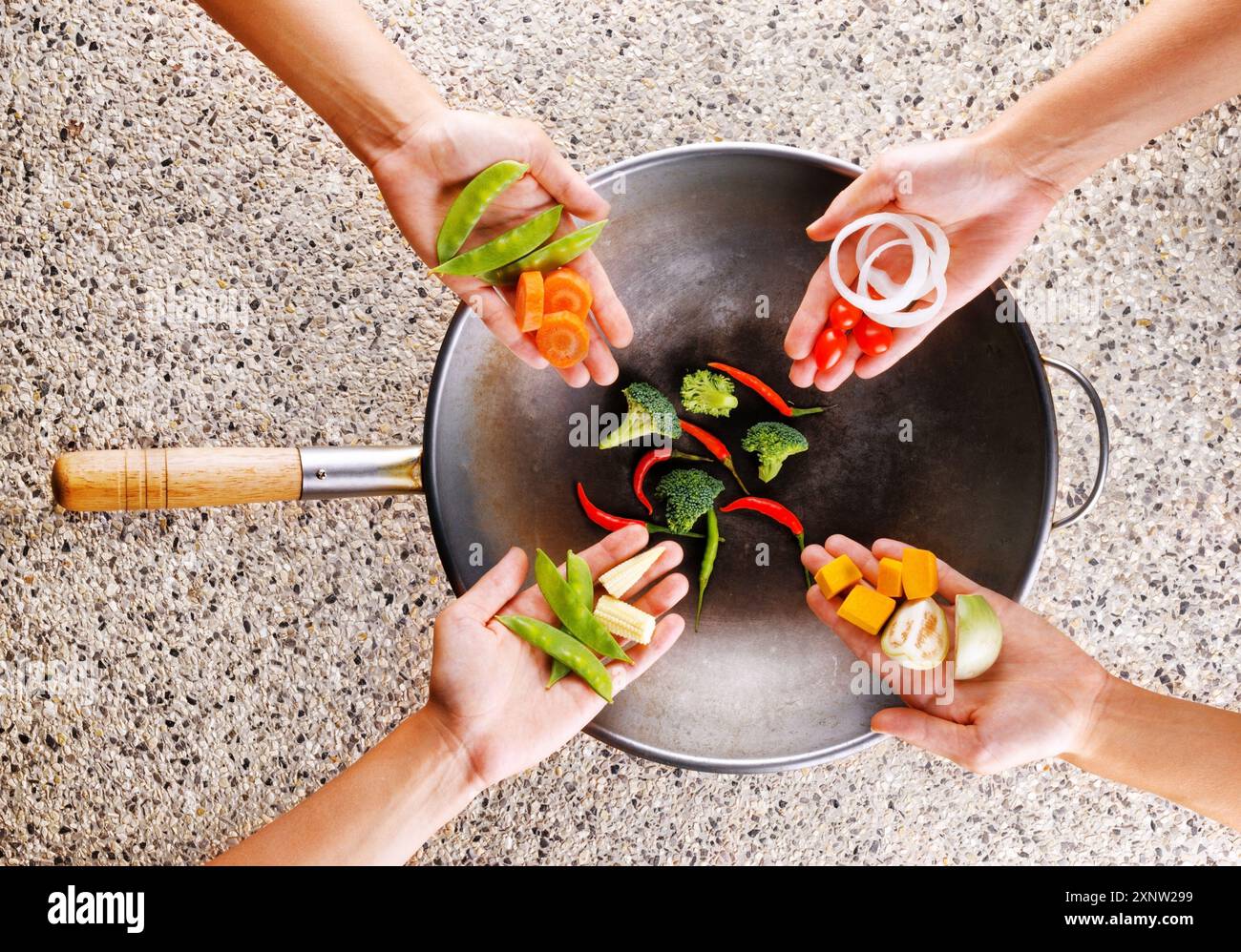 Four hands puts fresh vegetables in the wok. Cooking concept Stock ...