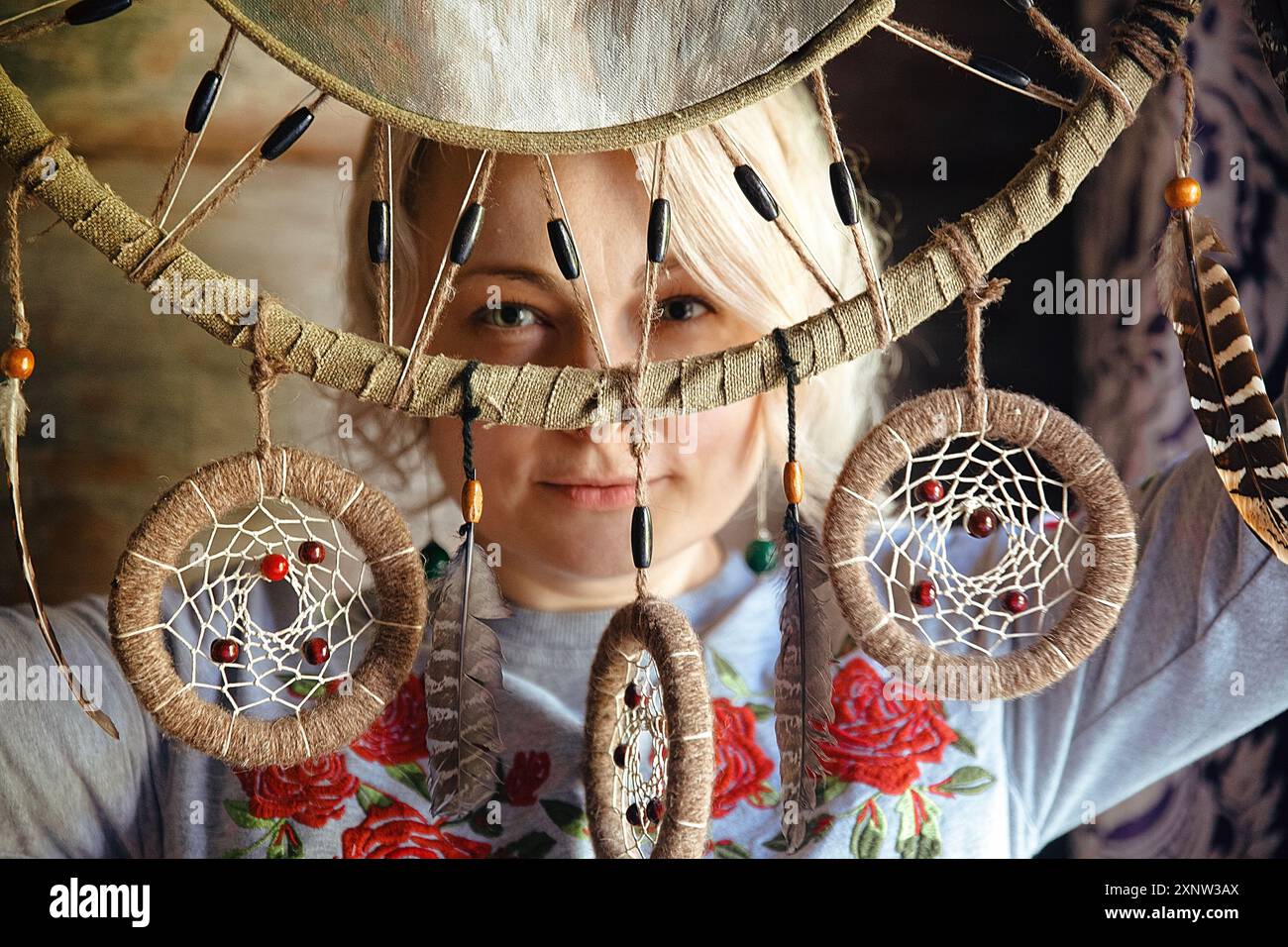 A woman with a soulful look holds a large dream catcher in front of her ...