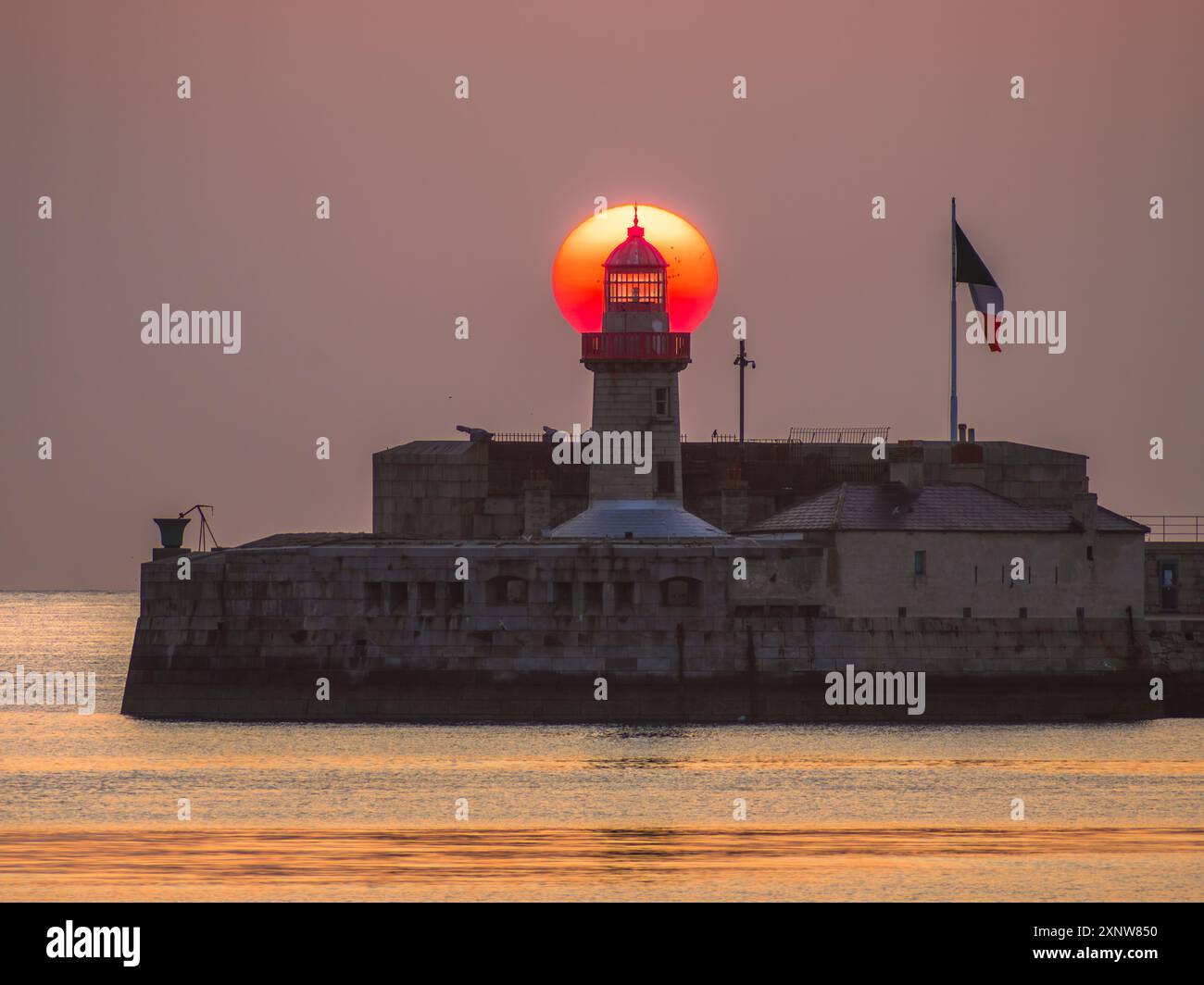 Hazy red sun rising behind Dún Laoghaire East Pier Lighthouse Stock ...