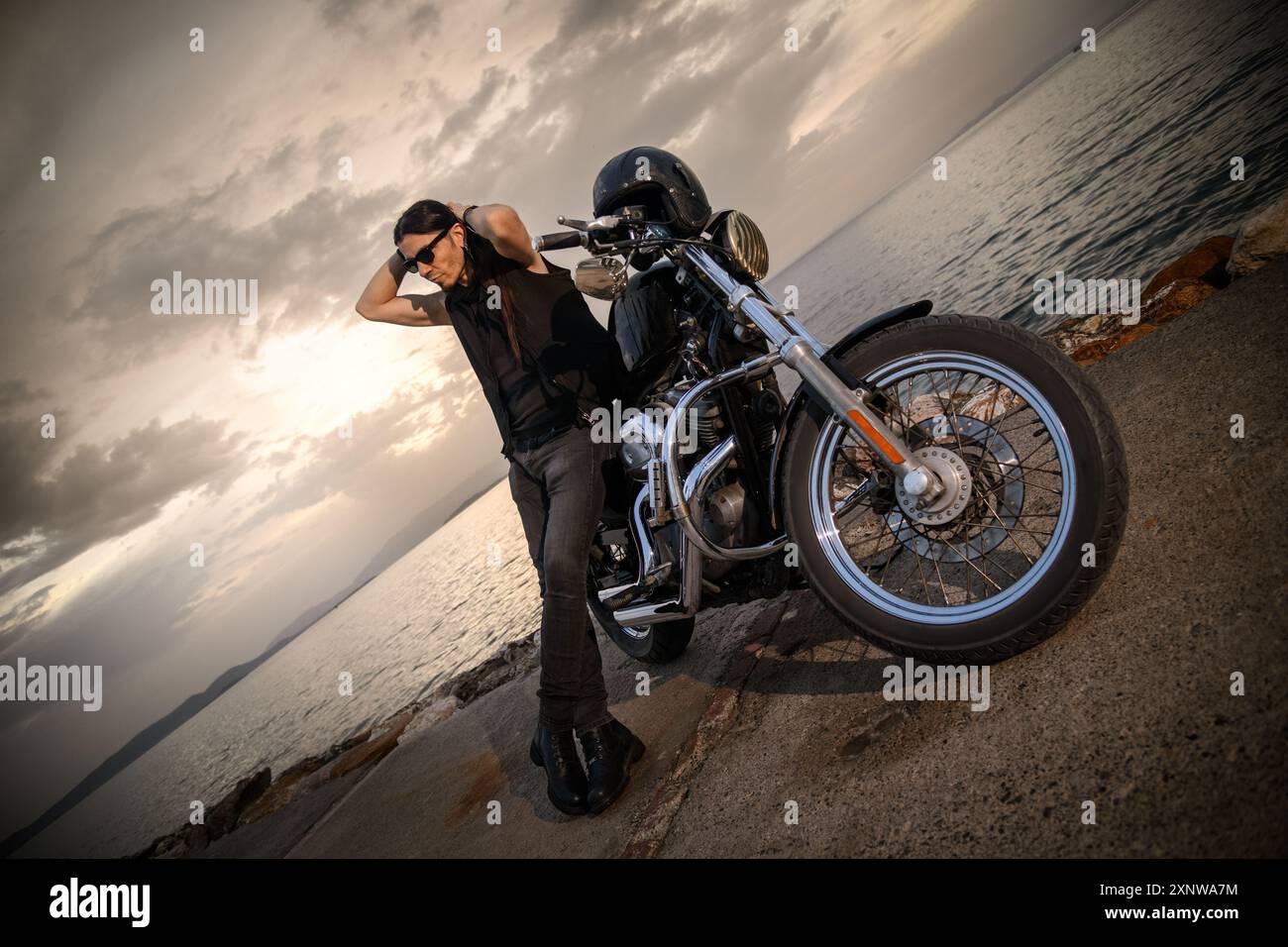 A biker with long hair leaning on his chopper-style motorcycle by the ...